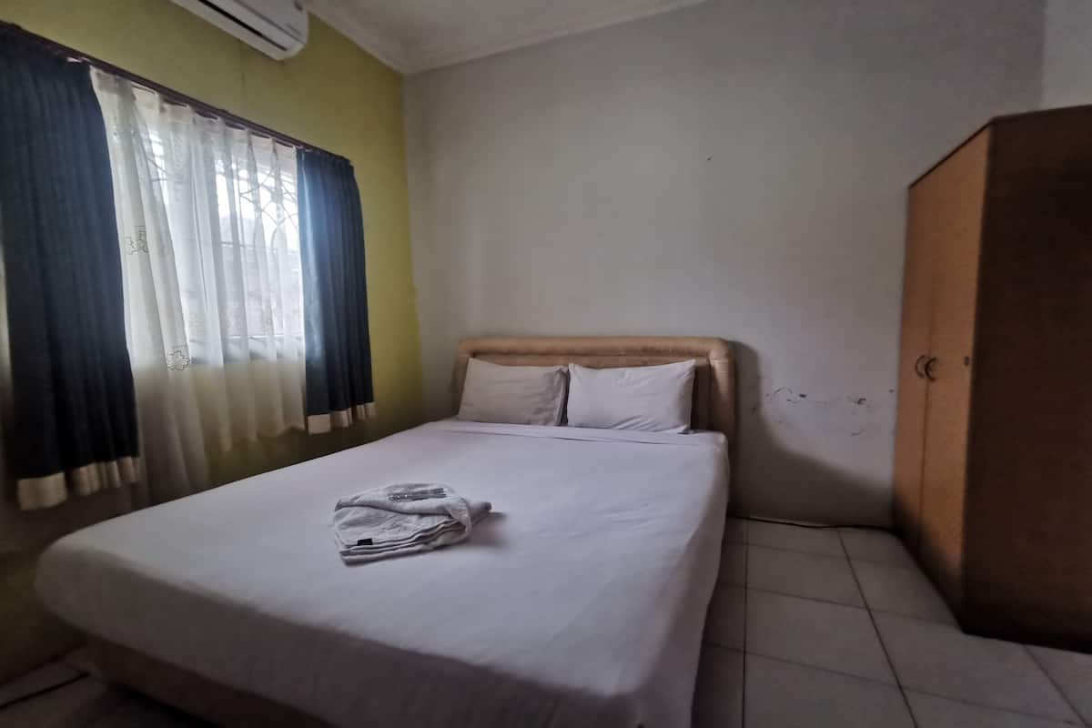 Uma cama de solteiro com colchão e travesseiros brancos, cabeceira de madeira e guarda-roupa de madeira.