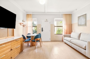 Uma sala de estar moderna com sofá, área de jantar com mesa e cadeiras, televisão de tela plana e porta que dá para outro cômodo.