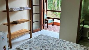 Quarto com estante de madeira, tapete estampado, televisão e vista para o verde lá fora.