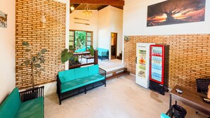 Um hall amplo com parede de tijolos, um sofá verde-água, um refrigerador Stella Artois e uma pintura de um pôr do sol.