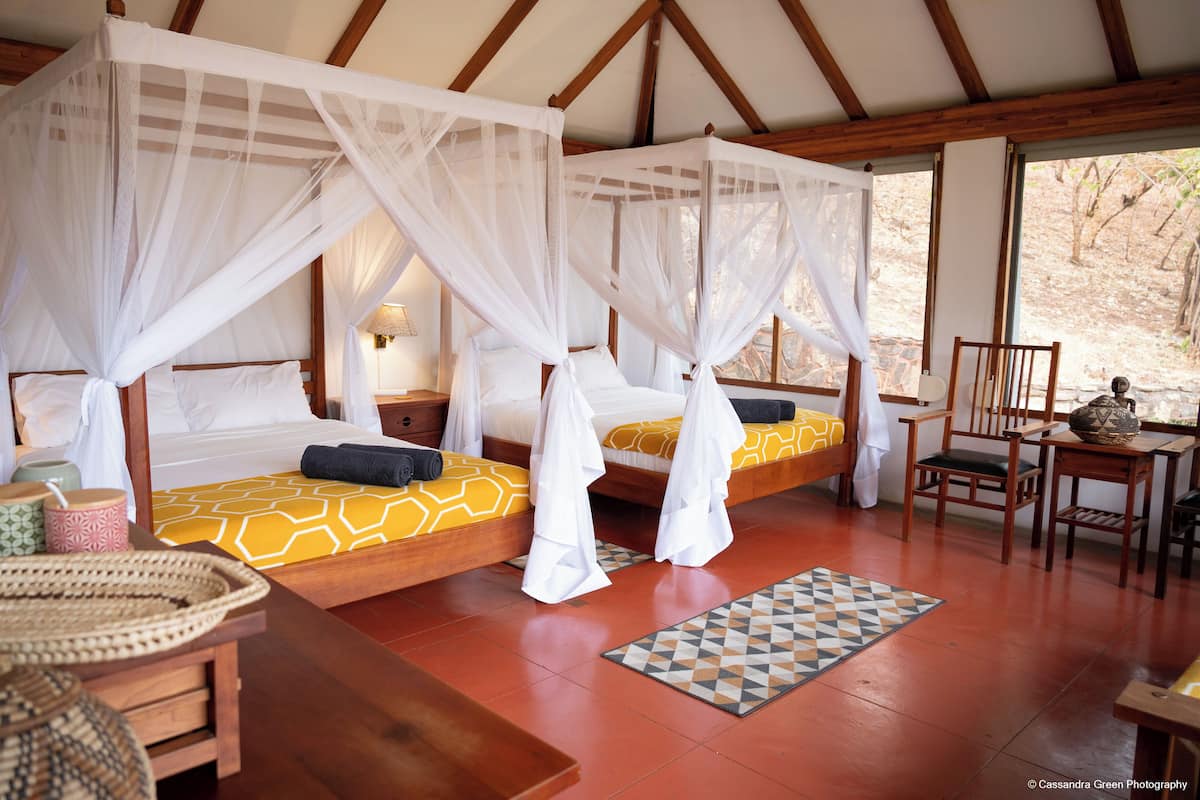 Quarto com duas camas, cada uma com dossel, mobiliário de madeira e vista para o exterior.