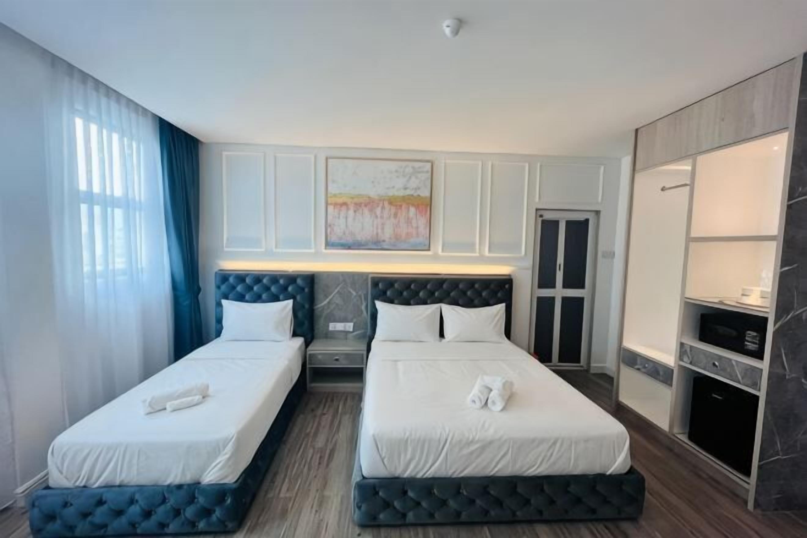 Quarto de hotel com duas camas, uma escrivaninha, um guarda-roupa e um quadro na parede.