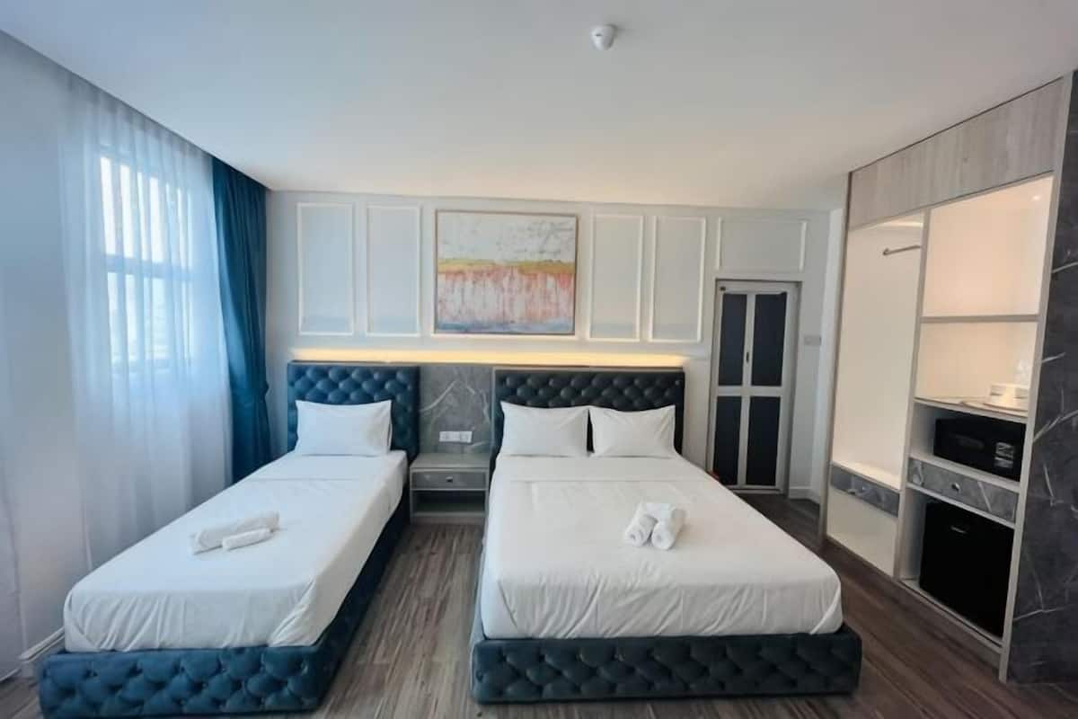 Quarto de hotel com duas camas, uma escrivaninha, um guarda-roupa e um quadro na parede.