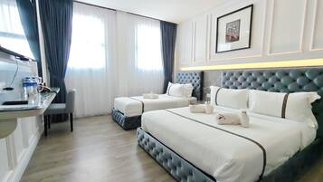 Quarto de hotel com uma cama grande, uma cama menor, uma escrivaninha com cadeira e uma janela com cortinas.