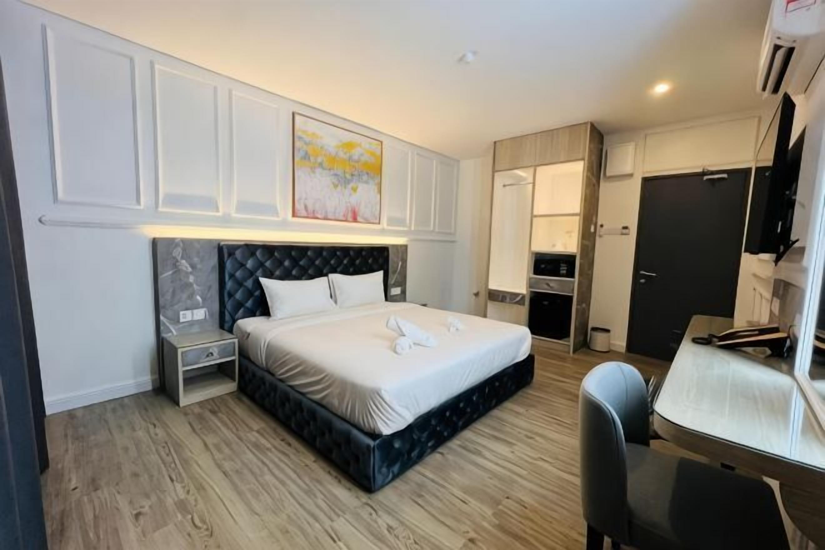 Quarto de hotel com cama, escrivaninha, cadeira, mesa de cabeceira e um quadro na parede.