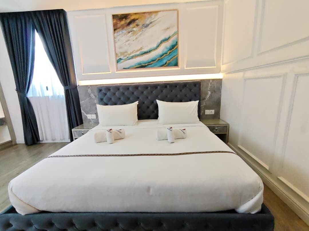 Uma cama bem arrumada com cabeceira estofada, roupa de cama branca e duas almofadas.