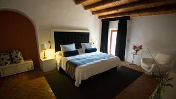 Quarto com uma cama grande, mesa de cabeceira com abajur, cadeira e vaso com flores.