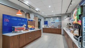 Uma área de café da manhã moderna com um painel de menu digital, uma exposição de frutas e um espaço para café.