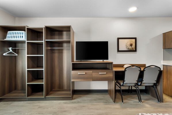 Quarto moderno com escrivaninha de madeira, duas cadeiras, uma TV e um guarda-roupa com prateleiras e espaço para pendurar roupas.