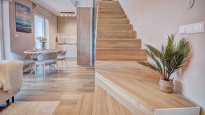 Interior moderno com escada de madeira, área de refeições com cadeiras e mesa, e cozinha ao fundo.