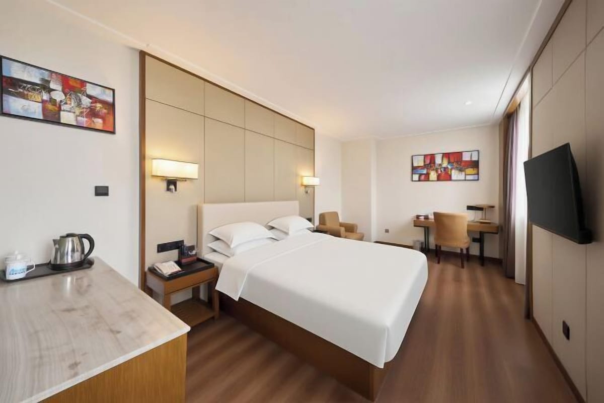 Quarto de hotel com uma cama grande, mesas de cabeceira, escrivaninha, cadeira e televisão.