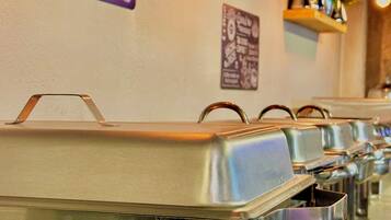 Buffet com bandejas de aço inoxidável e parede com sinalização sobre café.