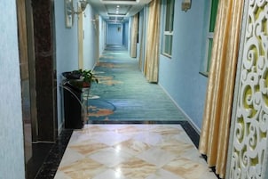Corredor de hotel com carpete estampado, planta em vaso e cortina decorativa.