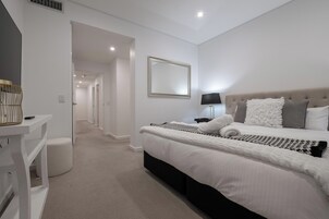 Quarto moderno com uma cama grande, mesa de cabeceira, abajur e espelho.