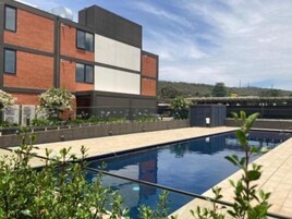 Um edifício moderno com piscina, rodeado por vegetação e um céu limpo.