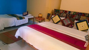 Quarto com duas camas, uma com colcha vermelha e a outra com colcha branca. Há uma pequena mesa com um recipiente amarelo e um quadro emoldurado.
