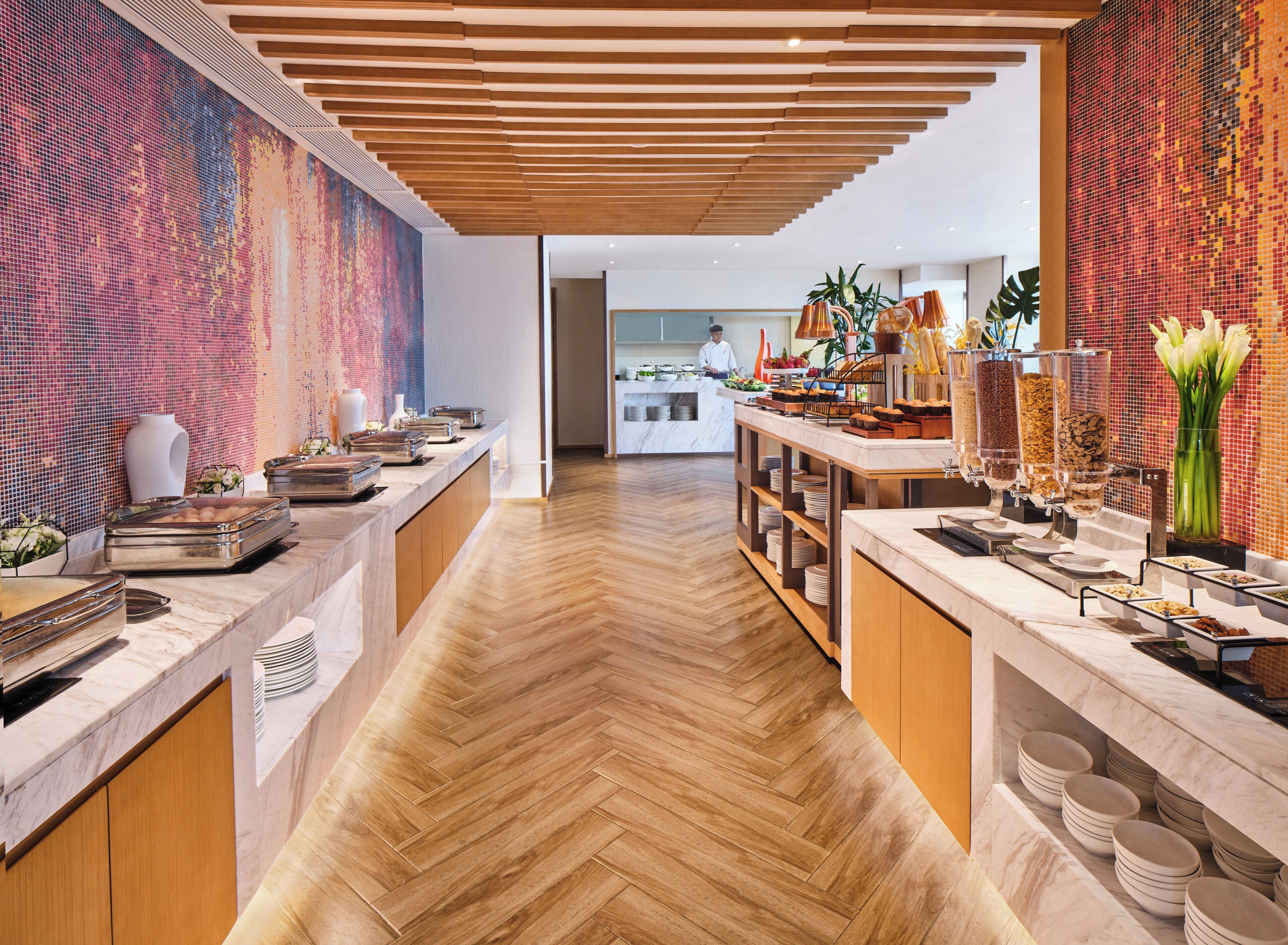 Uma área de buffet moderna com piso de madeira, bancadas de mármore e uma parede colorida em mosaico.