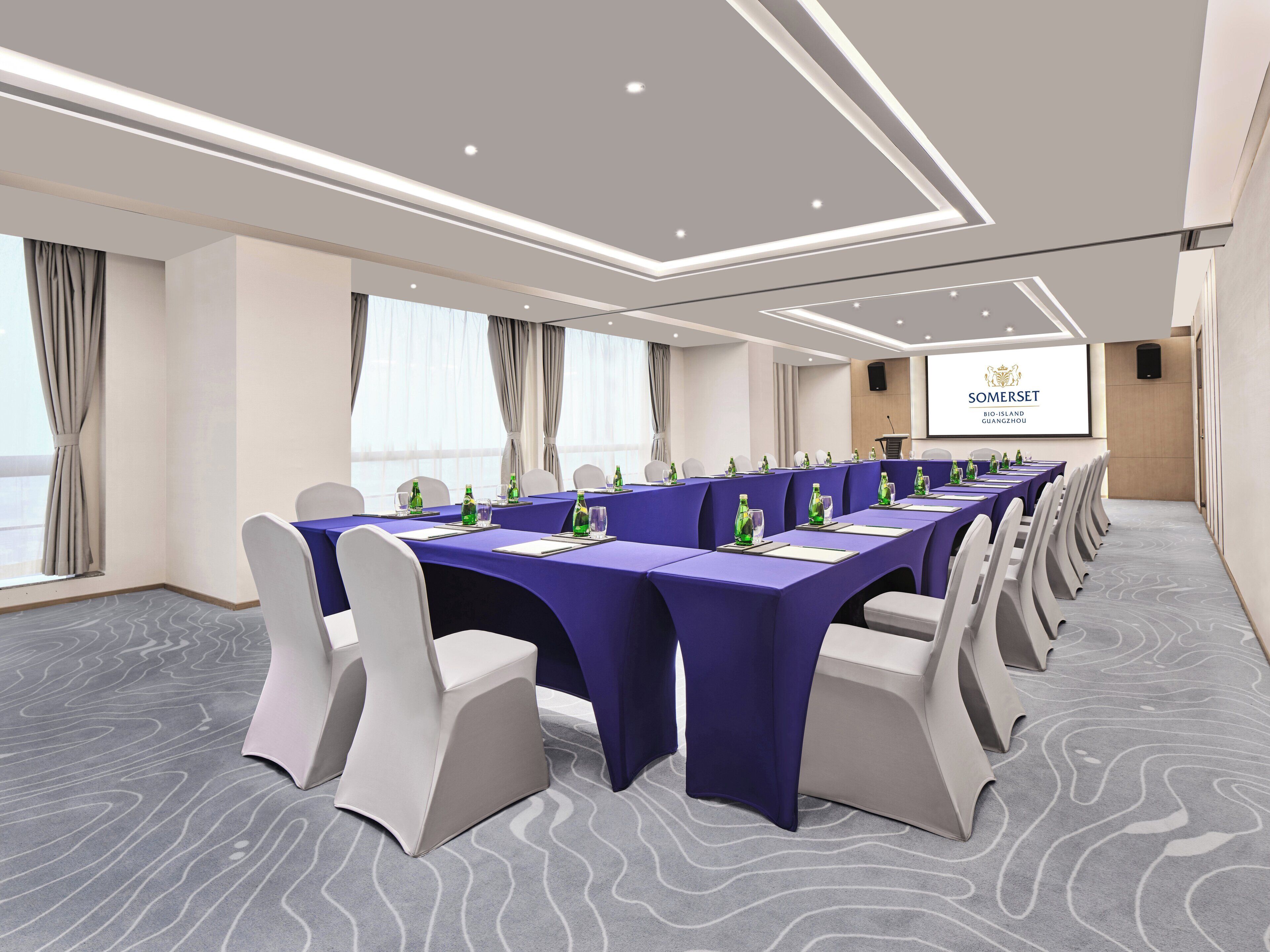 Uma sala de conferências com uma mesa comprida, cadeiras brancas e uma tela exibindo 'SOMERSET BIO-ISLAND GUANGZHOU'.