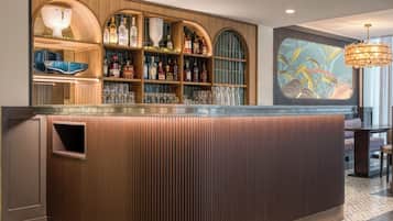 Uma área de bar com prateleiras de madeira, uma grande tigela decorativa e um mural de folhas tropicais.