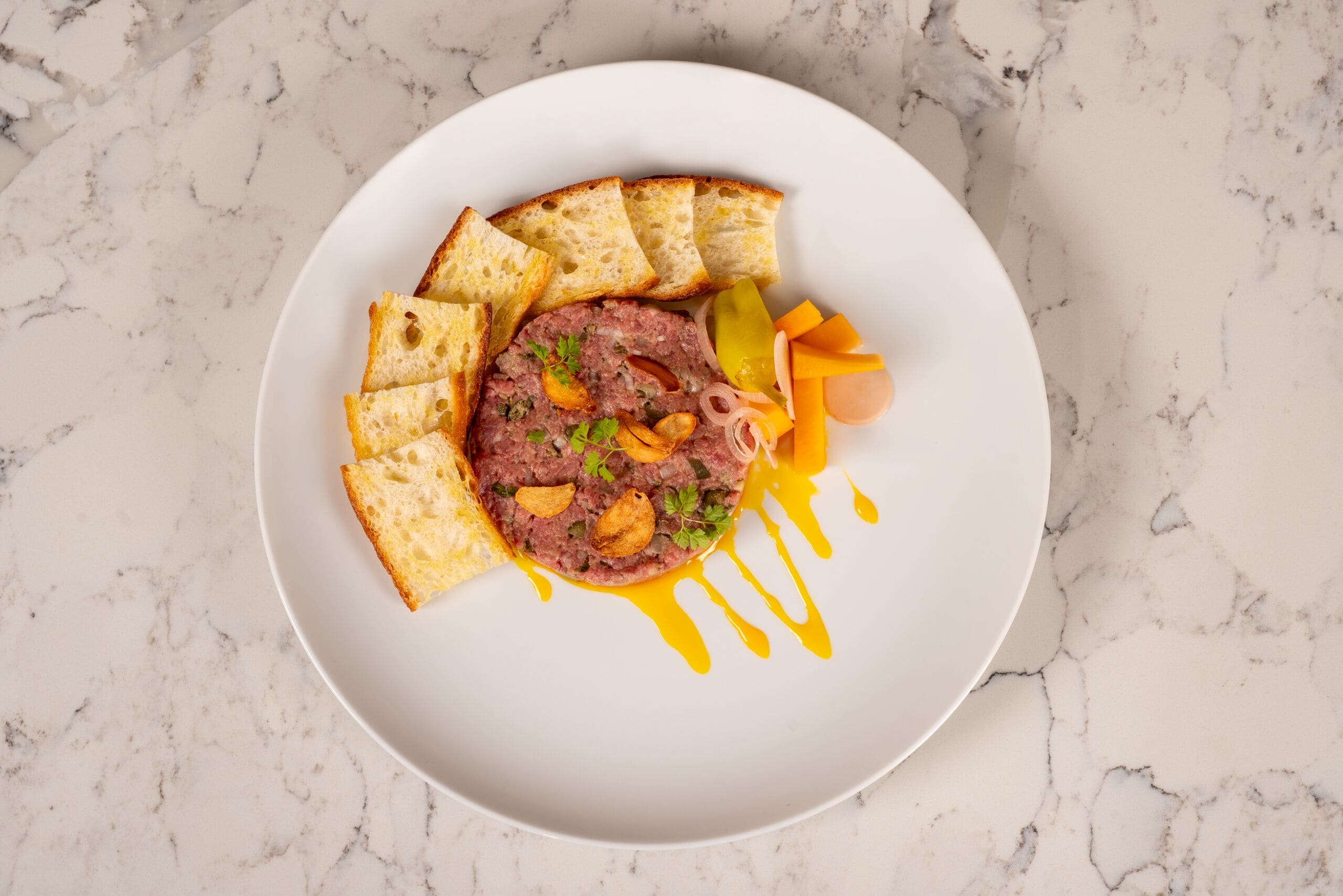 Um prato branco com prato de carne, picles e pão sobre uma superfície de mármore.