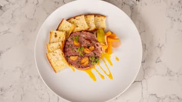 Um prato branco com prato de carne, picles e pão sobre uma superfície de mármore.