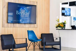 Uma área de recepção com o letreiro Bayside Suites, duas cadeiras pretas, uma parede de madeira e uma tela de televisão.