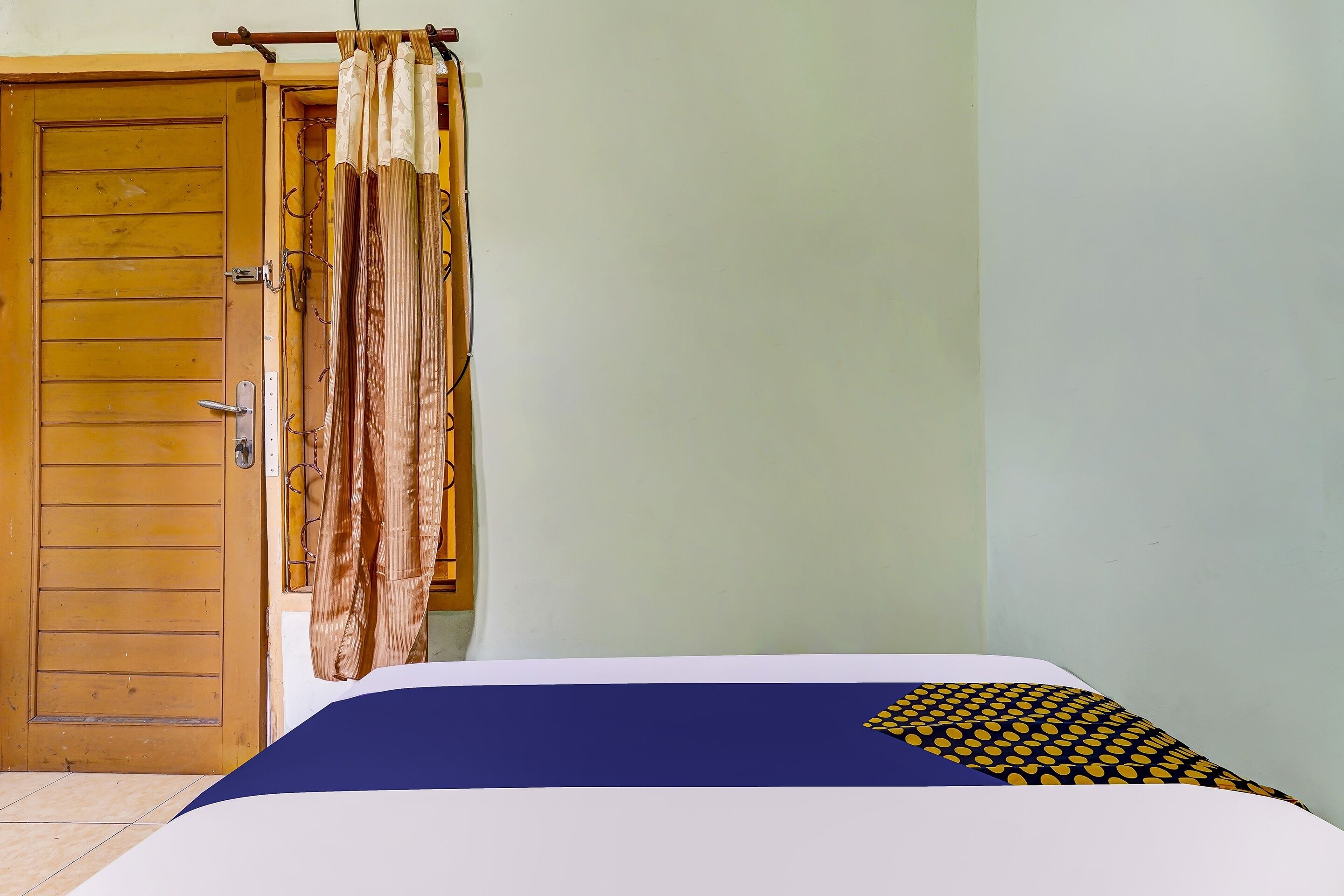 Quarto com porta de madeira, cama com colcha estampada em azul e amarelo, e cortina pendurada na porta.
