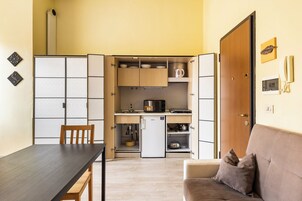 Cozinha compacta com frigorífico, micro-ondas e pia. Há uma mesa de jantar com cadeiras e um sofá na área de estar.