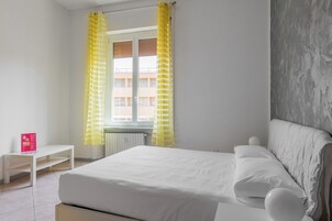 Quarto com cama, mesa de cabeceira e janela com cortinas amarelas.