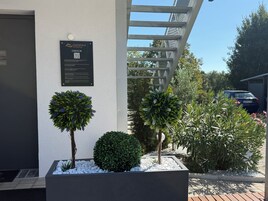 Entrada de um prédio com um código QR para registro, uma placa com o nome Gastehaus Estenfeld e dois vasos de plantas com pedrinhas brancas.