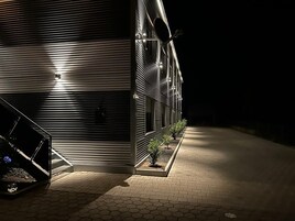 Um edifício moderno com fachada metálica, uma escadaria e pequenas plantas ao longo do caminho.