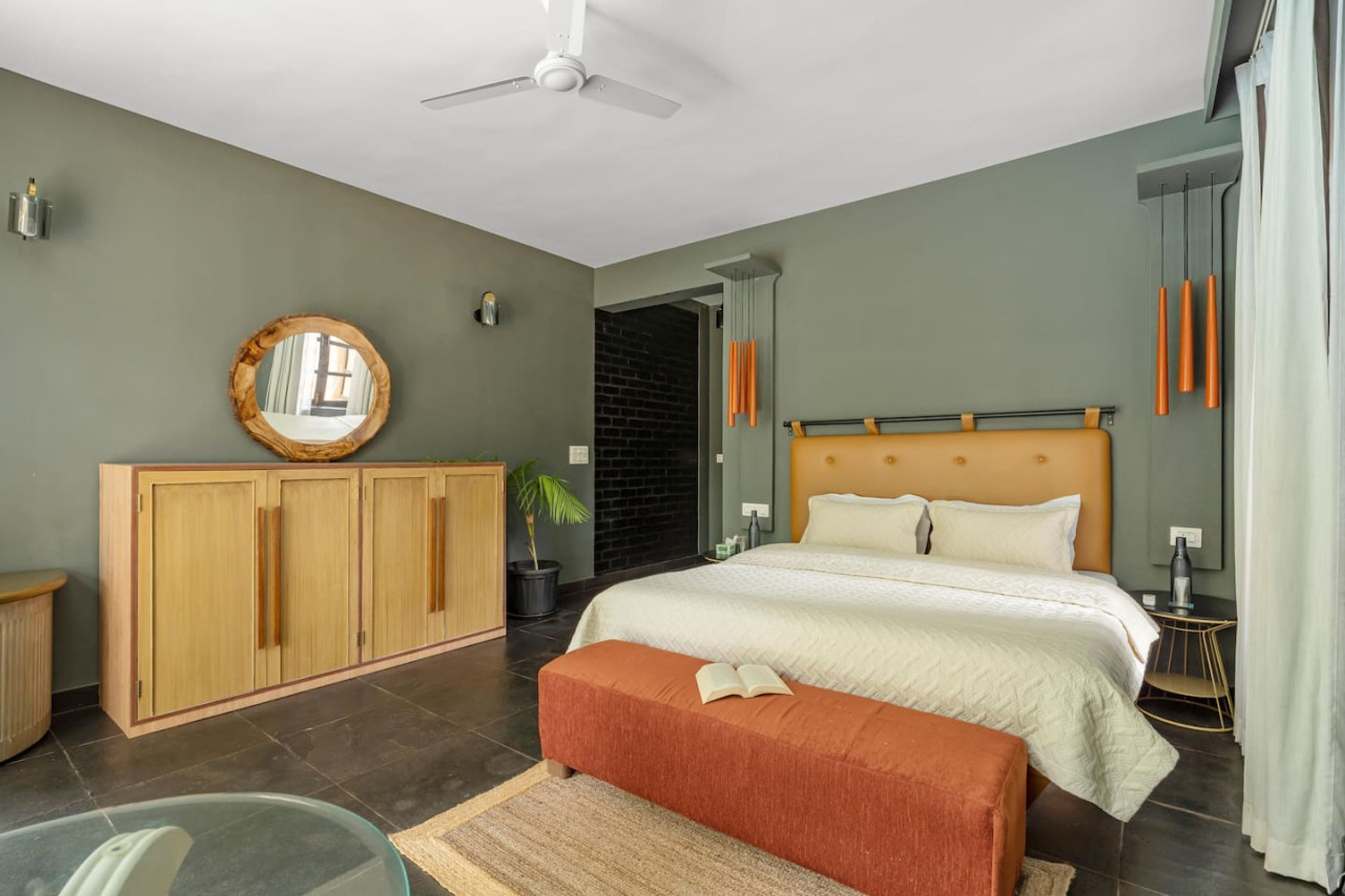 Quarto moderno com uma cama grande, um guarda-roupa de madeira, um espelho redondo e um ventilador de teto.