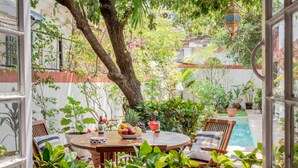 Uma mesa de madeira redonda com cadeiras, cercada por vegetação exuberante e uma pequena piscina.