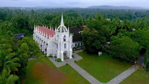 Um edifício de estilo colonial branco com uma torre central e telhado vermelho, rodeado por vegetação exuberante e palmeiras.