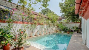 Piscina rodeada por plantas em vasos e uma cerca branca.