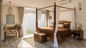 Uma cama com dossel de madeira com cortinas brancas, uma escrivaninha com cadeira, uma mesa de cabeceira com abajur e um mapa na parede.
