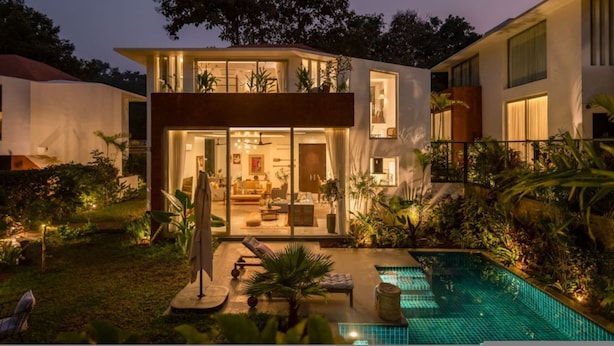 Uma casa moderna de dois andares com piscina, rodeada por vegetação exuberante.