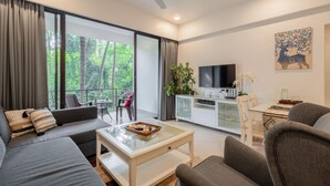 Sala moderna com sofá, mesa de centro e televisão. Tem uma varanda com vista para árvores.
