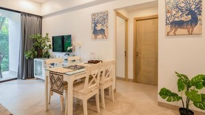 Uma sala de jantar moderna com uma mesa, cadeiras e uma televisão. Há duas pinturas na parede, uma porta e uma planta.