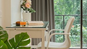 Quarto moderno com uma mesa de vidro, uma cadeira branca e vista para o verde lá fora.