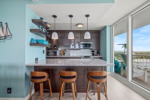 Uma cozinha moderna com uma ilha grande, banquetas, luminárias pendentes e vista para o oceano.