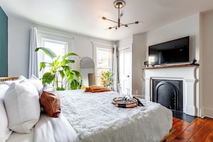 Um quarto com cama, lareira, televisão e uma janela grande.