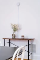 Um quarto minimalista com uma mesa de madeira, um vaso com flores e um pequeno frasco decorativo.