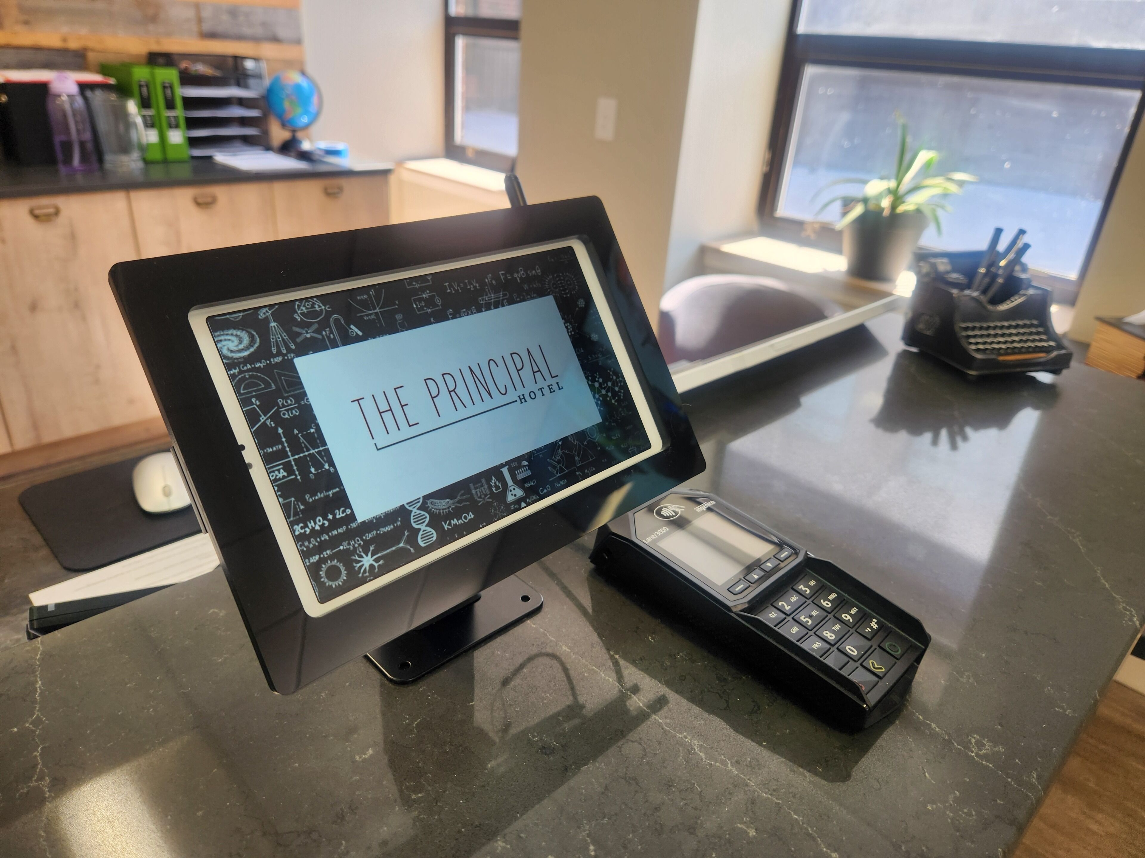 Uma mesa com um monitor de computador exibindo 'THE PRINCIPAL HOTEL' e uma calculadora.