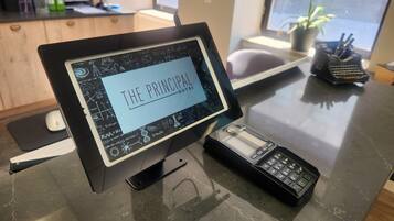 Uma mesa com um monitor de computador exibindo 'THE PRINCIPAL HOTEL' e uma calculadora.