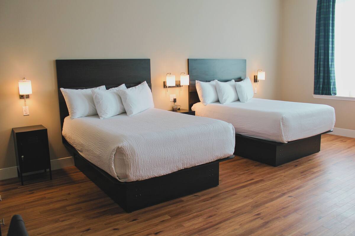 Quarto de hotel com duas camas, piso de madeira e abajures.