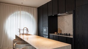 Uma cozinha moderna com uma ilha grande, armários escuros e uma janela ampla com cortinas leves.