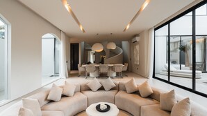 Uma sala de estar moderna com um amplo sofá de canto, uma área de jantar com cozinha sinuosa e grandes janelas com vista para o exterior.