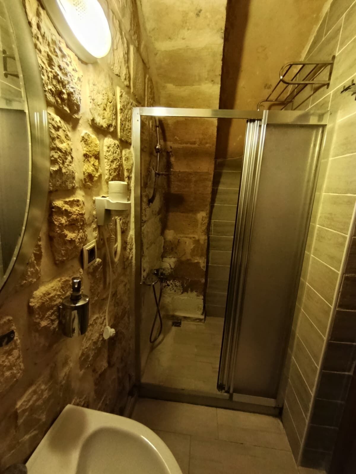 Casa de banho com parede de pedra, cabine de duche em vidro e lavatório branco.