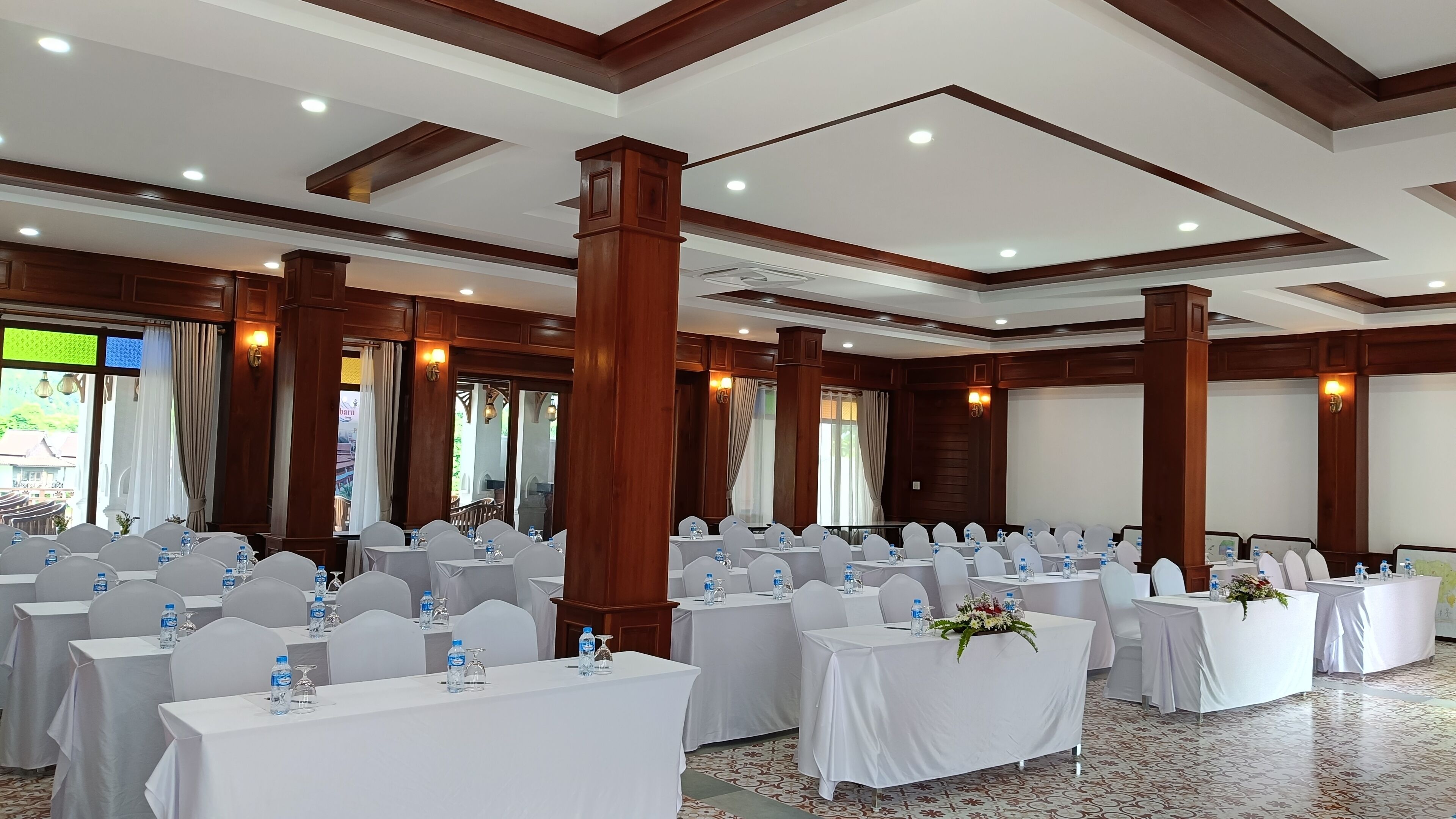 Sala de conferência com várias mesas, cadeiras brancas e garrafas de água.
